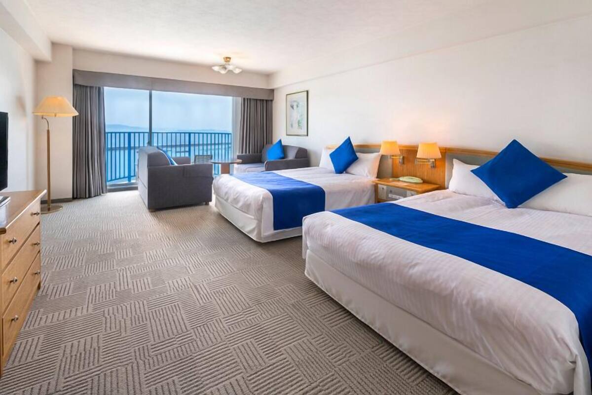Quarto de hotel com duas camas, um sofá, uma televisão e uma varanda com vista.