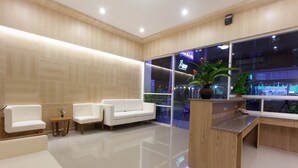 Um lobby moderno com sofás brancos, um balcão de recepção de madeira e janelas amplas.