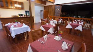 Restaurante com várias mesas preparadas para refeições, cadeiras de madeira e um bar ao fundo.