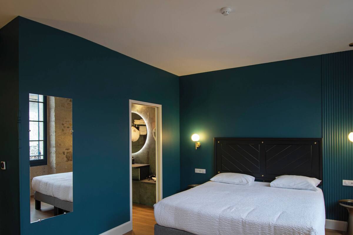 Quarto moderno com paredes verde-água, uma cama grande, um espelho e piso de madeira.