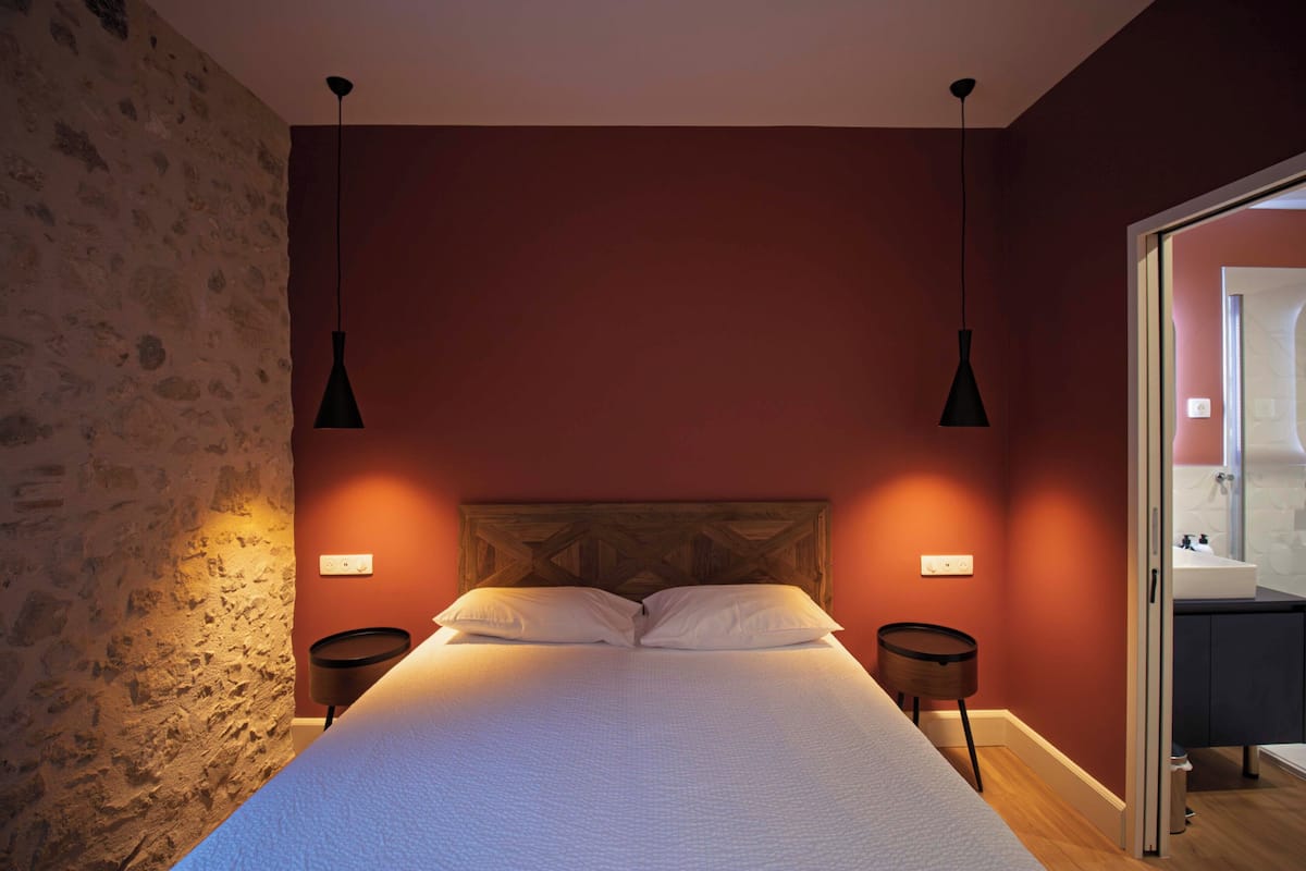 Quarto com uma cama grande, duas mesas de cabeceira, uma cabeceira de madeira e uma parede de pedra.