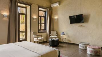 Quarto de hotel com cama, duas cadeiras, uma mesinha, televisão e janela com cortinas.