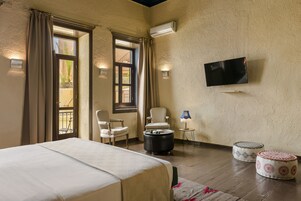 Quarto de hotel com cama, duas cadeiras, uma mesinha, televisão e janela com cortinas.