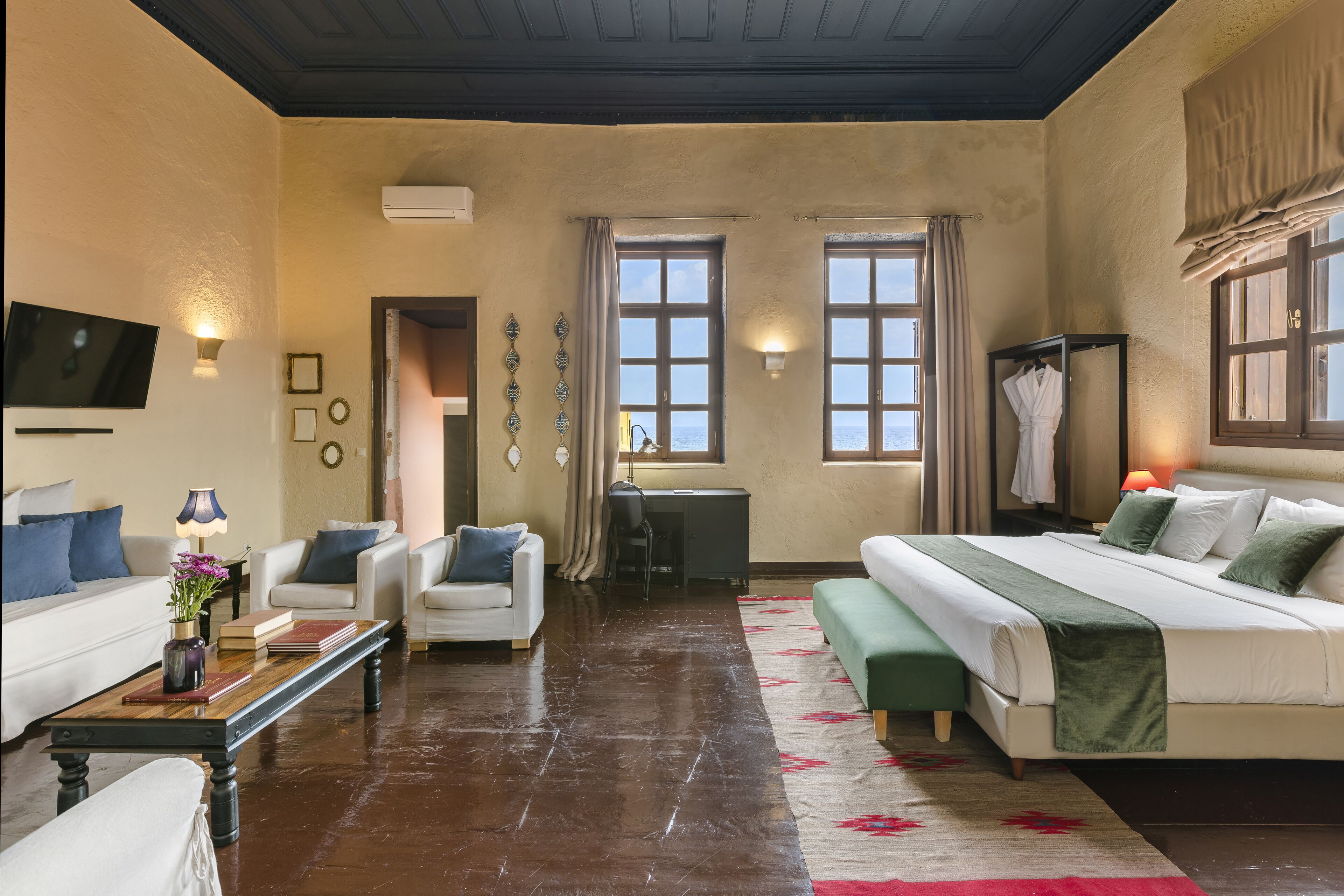 Quarto de hotel com cama, duas poltronas, escrivaninha e televisão.