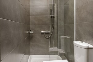 Um banheiro moderno com chuveiro em box de vidro, vaso sanitário branco e design elegante.
