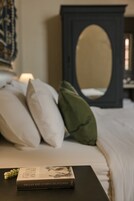Cama bem arrumada com um livro intitulado "The Art of War" e um pequeno buquê de flores em uma mesa de cabeceira.