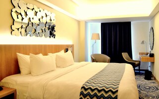 Quarto de hotel com uma cama grande, uma escrivaninha, uma cadeira e um espelho na parede.