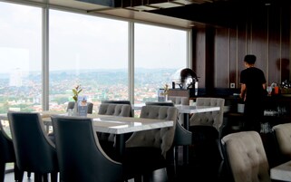 Um restaurante com vista para a cidade, mesas, cadeiras e um bar.