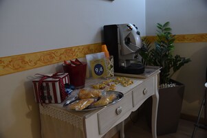 Uma mesa de buffet com comidas, uma máquina de café e uma planta.