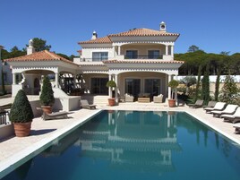 Uma casa de dois andares com piscina, área de estar externa e um jardim.