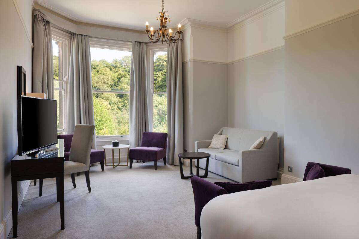 Quarto de hotel com cama, sofá, televisão e escrivaninha.