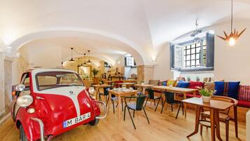 Um carro antigo estacionado em um café com mesas e cadeiras de madeira, um sofá e uma janela grande com vista.