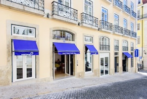 Uma fileira de edifícios com toldos azuis, cada um identificado como 'Lisbon Chiado Family Suites'.