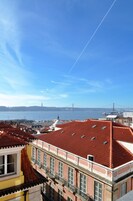 Paisagem costeira com edifícios de telhado vermelho, uma ponte em destaque ao longe, e céu claro.