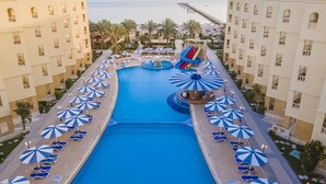Área de piscina em resort com escorrega, espreguiçadeiras e guarda-sóis.