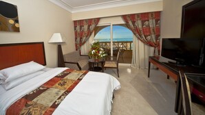 Quarto de hotel com cama, televisão, escrivaninha e vista para a praia.