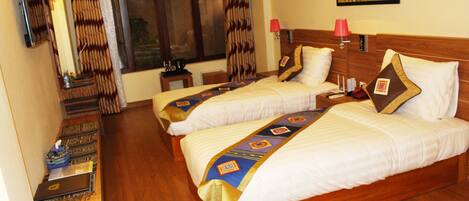 Quarto de hotel com duas camas, piso de madeira, uma janela grande com cortinas, uma obra de arte na parede e uma mesa de cabeceira com abajur.