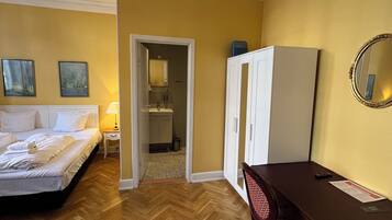 Quarto de hotel com cama, escrivaninha, cadeira, guarda-roupa, espelho e candelabro.