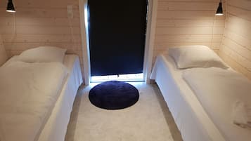 Quarto com duas camas de solteiro, um tapete redondo pequeno e uma janela com cortina escura.