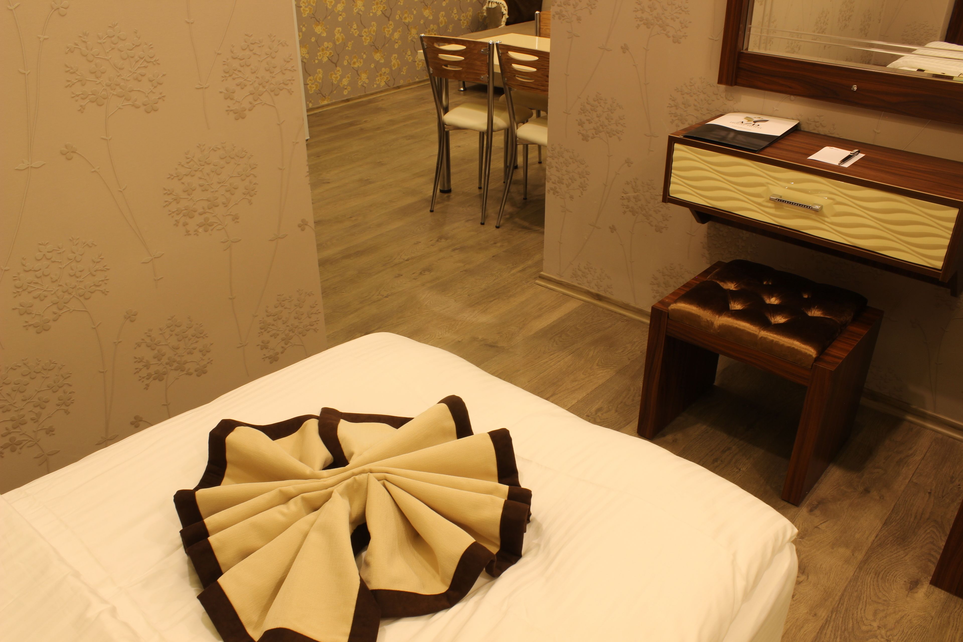 Quarto de hotel com cama bem arrumada, escrivaninha de madeira com cadeira e um banquinho pequeno.