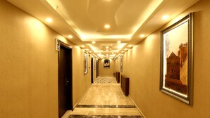 Corredor de hotel com piso de mármore, obras de arte emolduradas nas paredes e iluminação embutida.