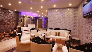 Uma área de estar luxuosa com assentos confortáveis, um balcão de recepção e uma tela grande.