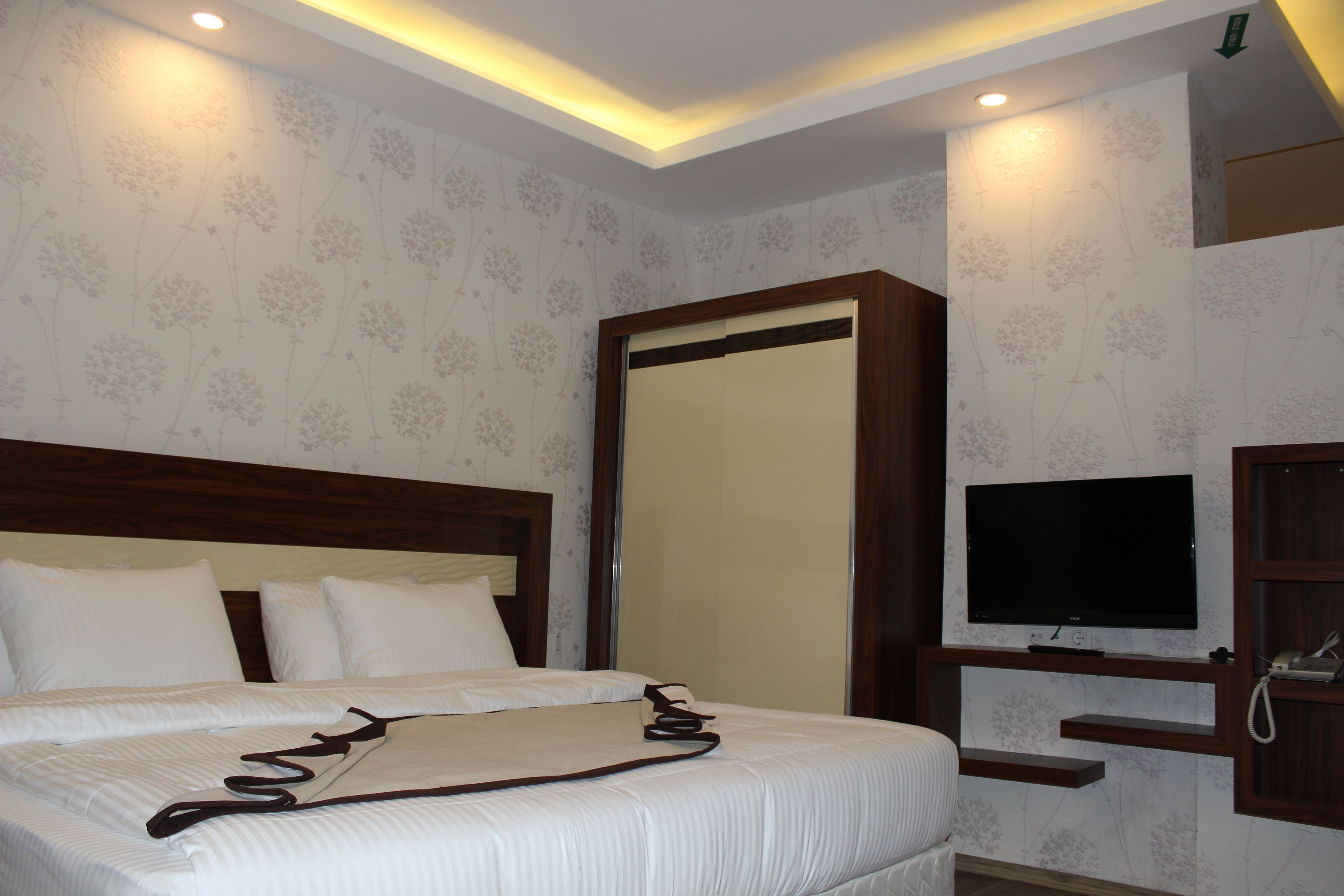 Quarto de hotel com uma cama grande, televisão de tela plana na parede e cabeceira de madeira.
