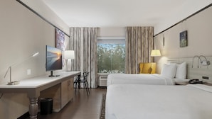 Quarto de hotel com cama, escrivaninha, cadeira e televisão.