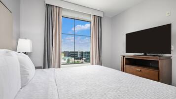 Quarto de hotel com uma cama grande, televisão, janela com cortinas e vista para edifícios.