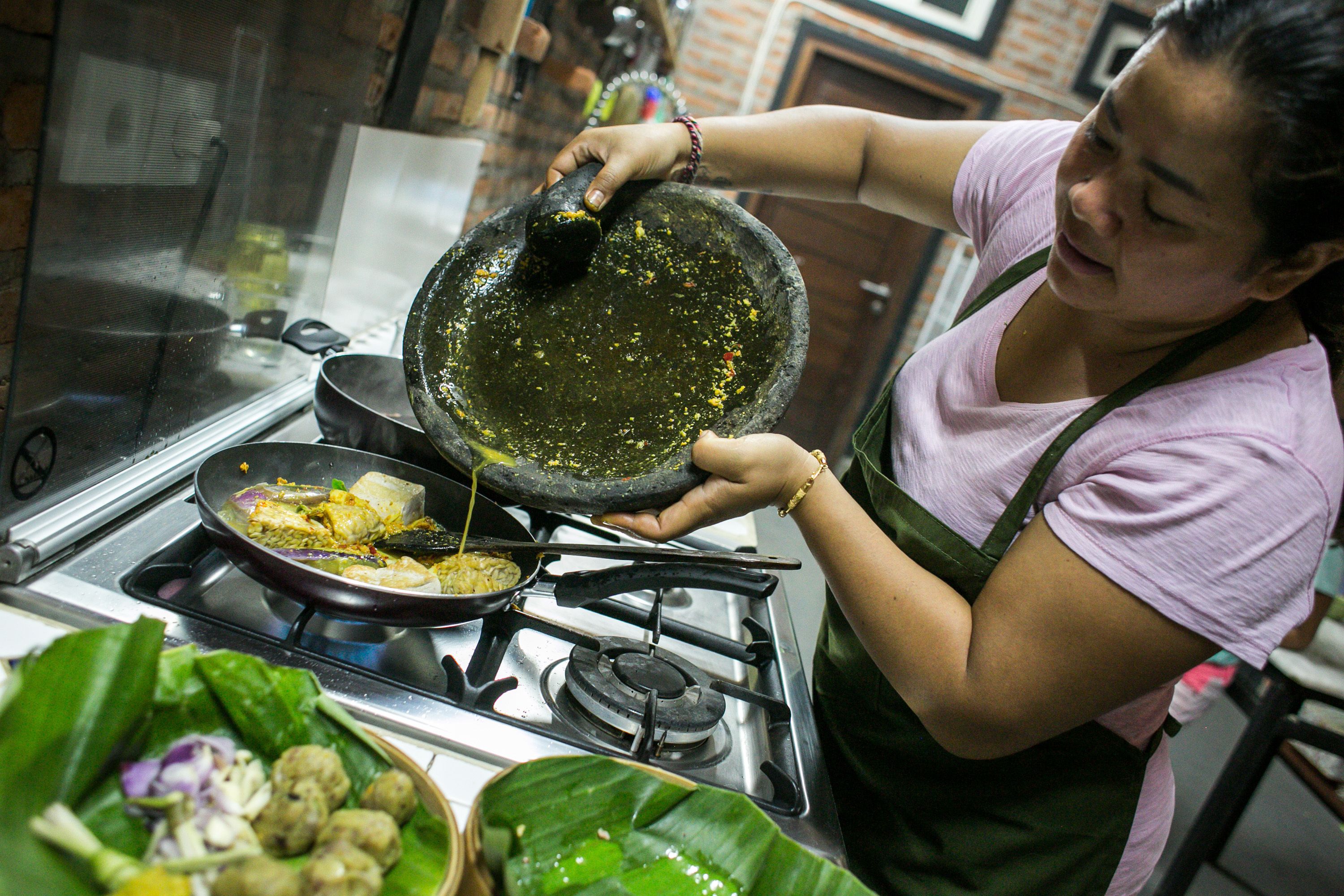 Uma pessoa cozinhando em um fogão, segurando uma frigideira com comida.