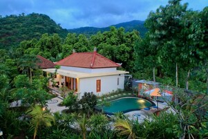 Uma villa com piscina cercada por vegetação exuberante e colinas ao fundo.