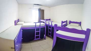 Quarto com três beliches, uma escrivaninha e uma janela com cortinas.