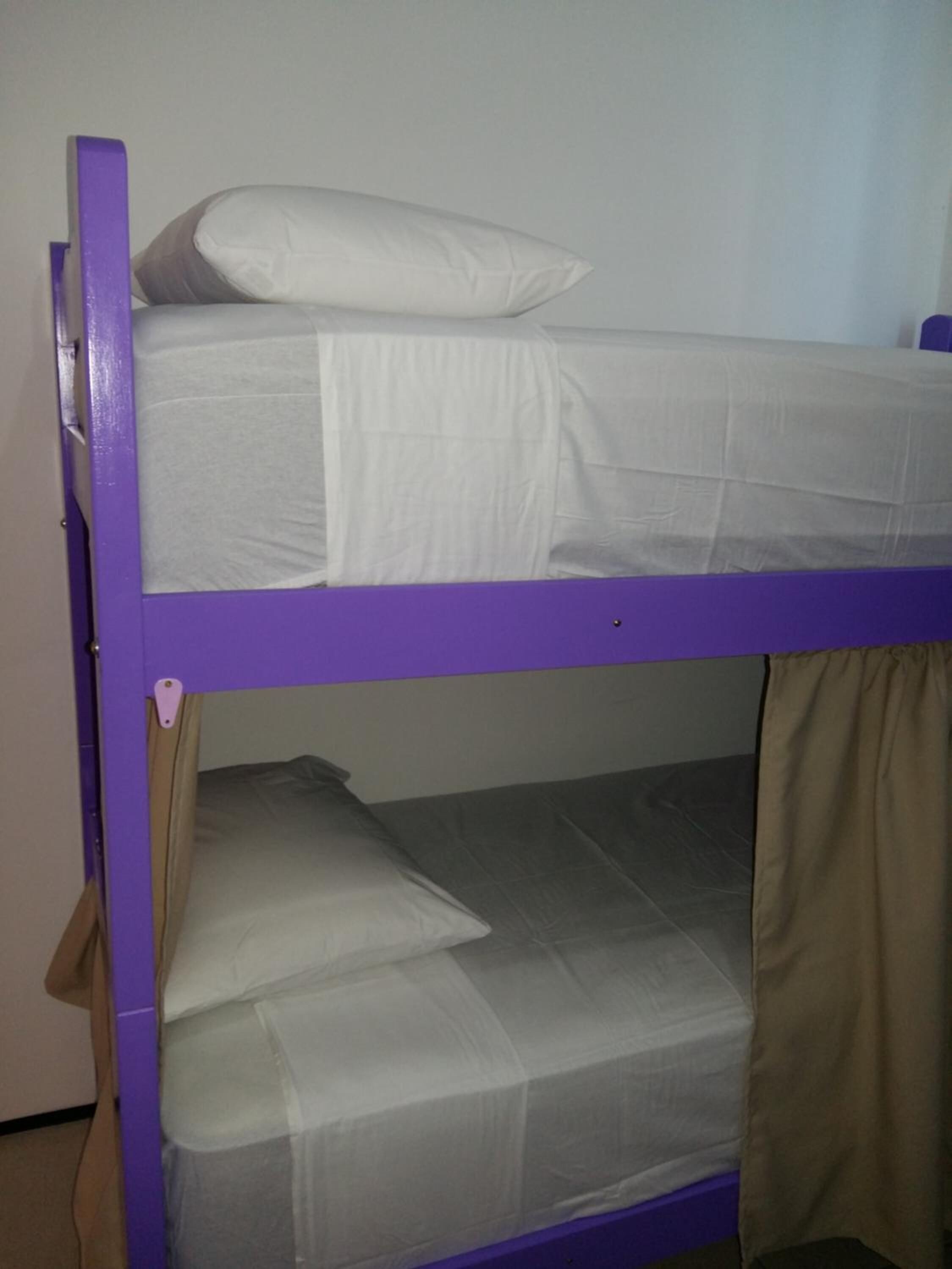 Uma cama beliche com estrutura roxa e roupa de cama branca.