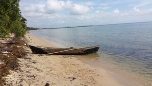 Um barco numa praia arenosa com água cristalina e uma linha de costa distante.
