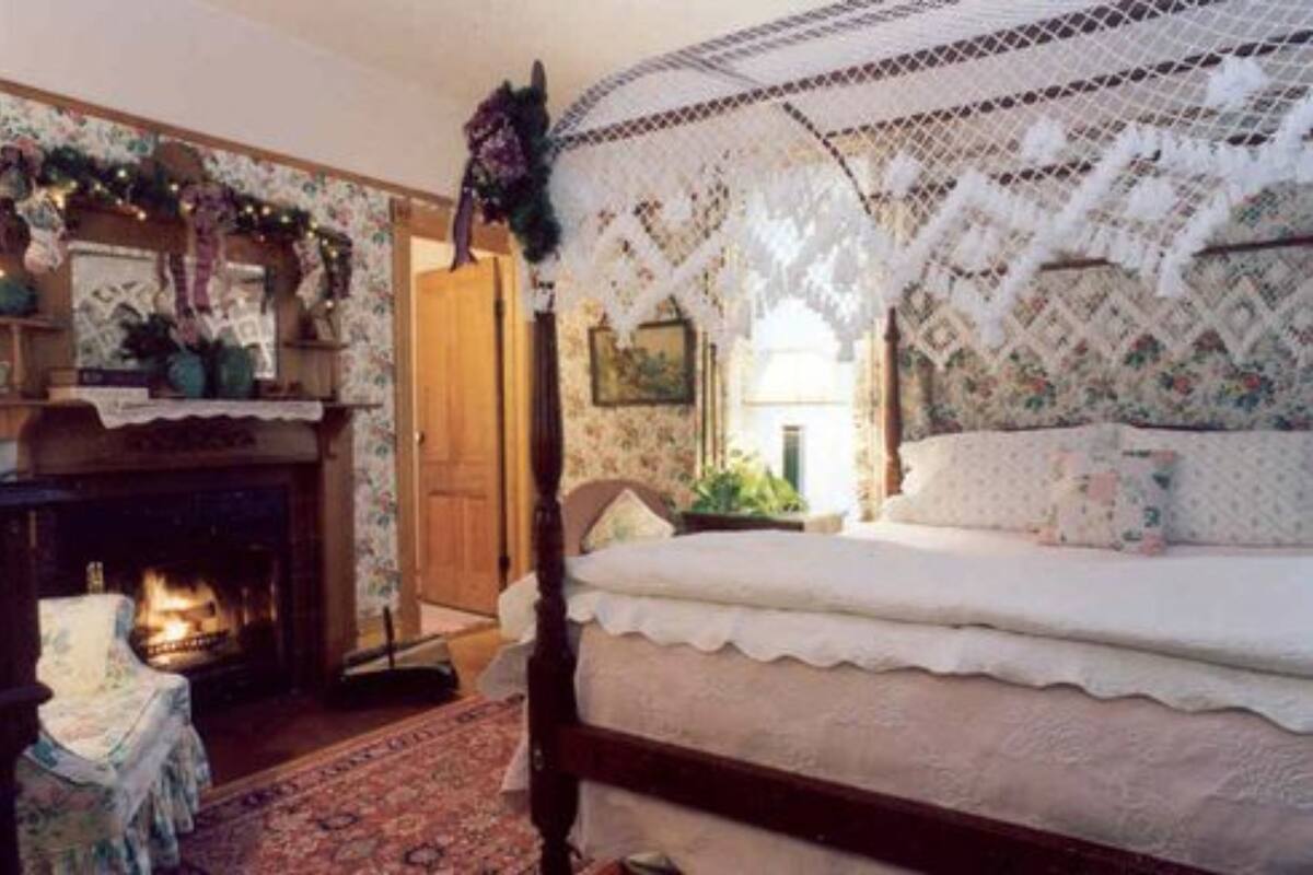 Quarto tradicional com cama de dossel, lareira e papel de parede floral.