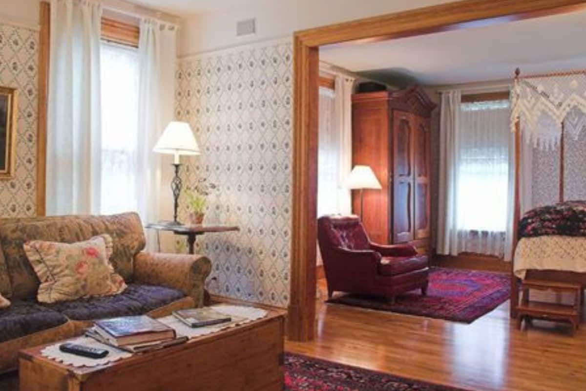 Uma sala de estar acolhedora com sofá, poltrona e mesa de centro. Apresenta um papel de parede estampado e piso de madeira.