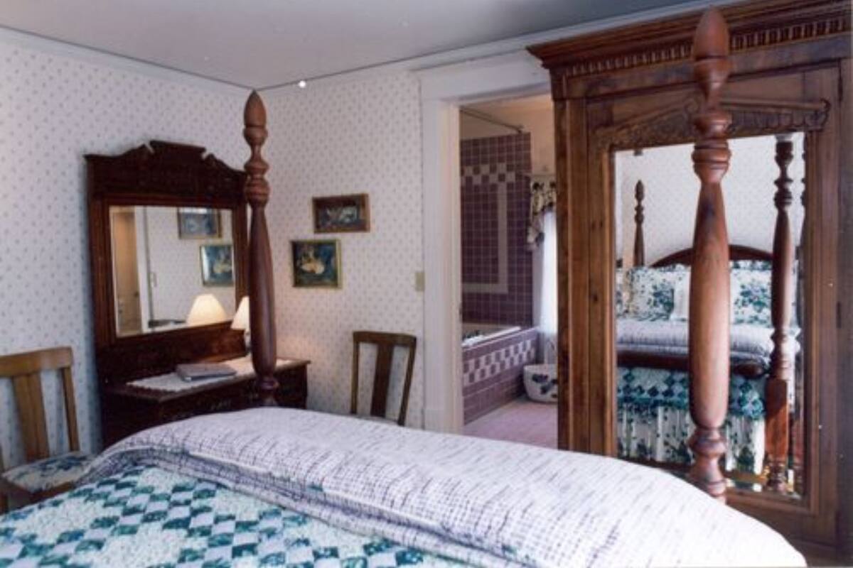 Quarto com cama de dossel, cómoda de madeira, espelho e mesa de cabeceira pequena.