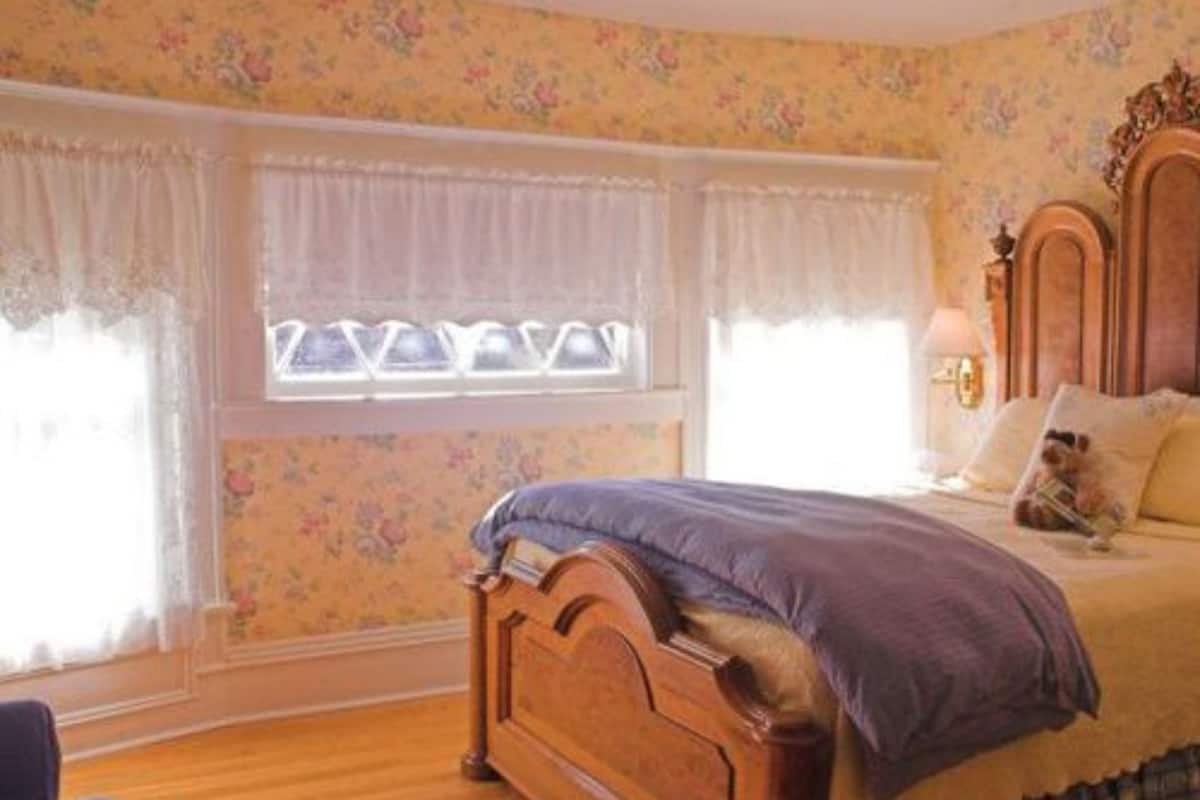 Quarto com cama de madeira, papel de parede floral e janela com cortinas.