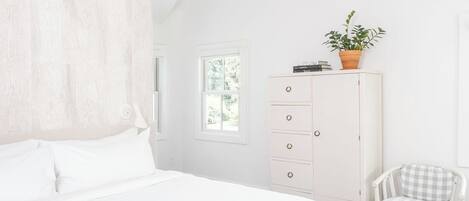 Quarto com uma cama grande, cômoda, cadeira e janela.