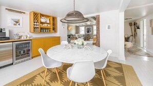 Cozinha moderna com mesa redonda de mármore, cadeiras brancas e armário amarelo com copos.