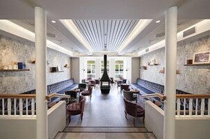Um hall de hotel com área de estar central, um piano de cauda e teto alto com padrão quadriculado.