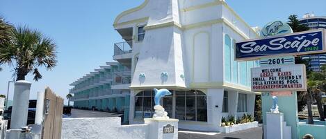 Um edifício branco com a placa do SeaScape Inn, com varandas e uma escultura de golfinho.