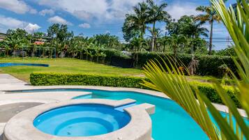 Uma piscina com design circular, rodeada por um gramado bem cuidado e palmeiras.