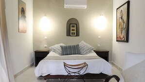Quarto com cama, mesas de cabeceira, uma cadeira, uma mesa redonda com flores e um tapete estampado.