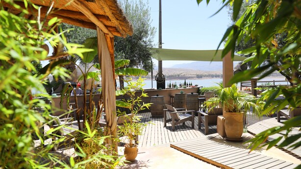 Um deck de madeira com área de estar externa, plantas em vasos e vista para a água.
