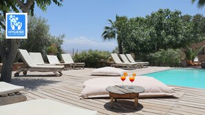 Uma área à beira da piscina com espreguiçadeiras, uma mesa de madeira com bebidas e um sinal de higiene.