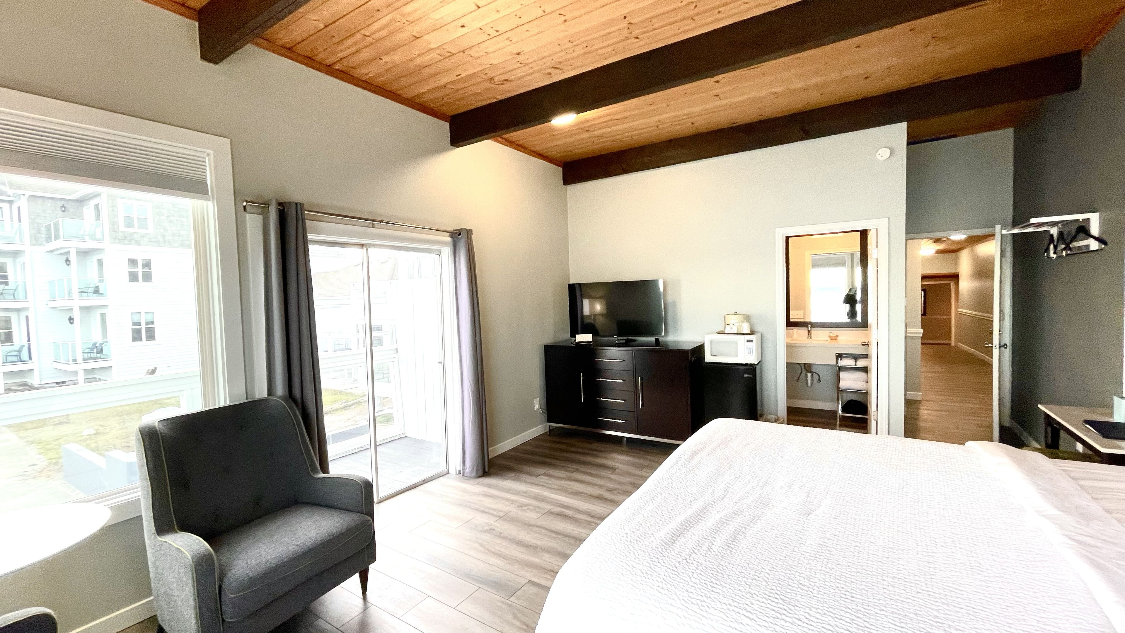 Quarto de hotel com cama, televisão, secretária e janela com vista para outros edifícios.