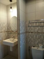 Casa de banho com lavatório, espelho, sanita e chuveiro.