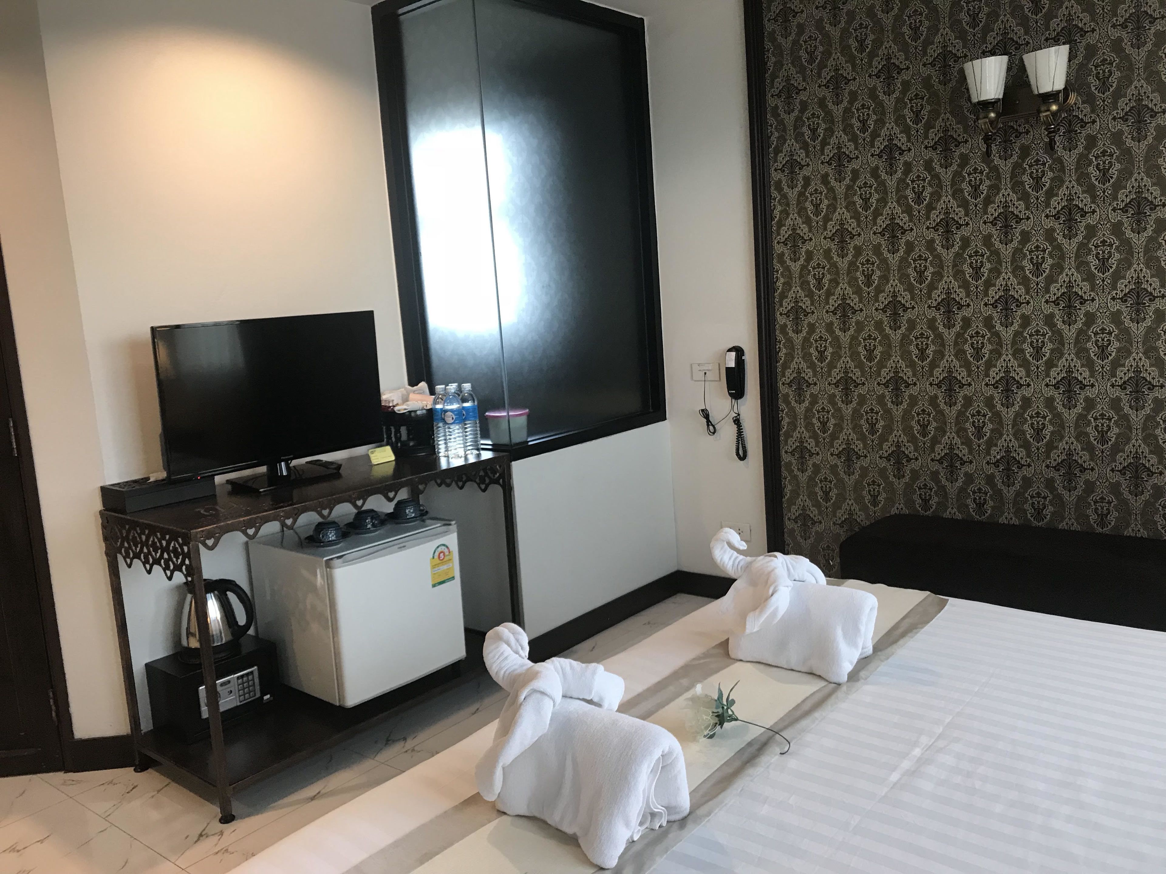 Quarto de hotel com cama, televisão, minibar, telefone e toalhas no chão.