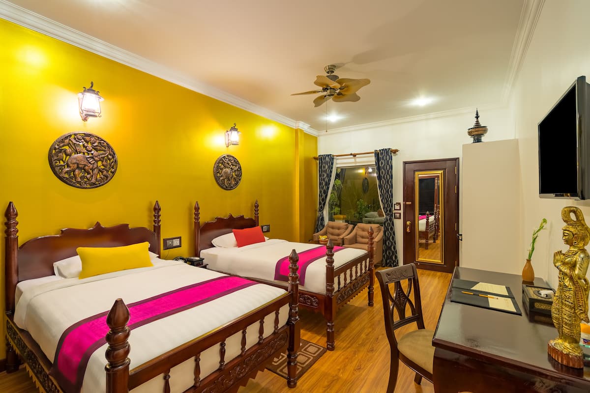 Quarto de hotel com duas camas de madeira, uma escrivaninha com televisão e um ventilador de teto.
